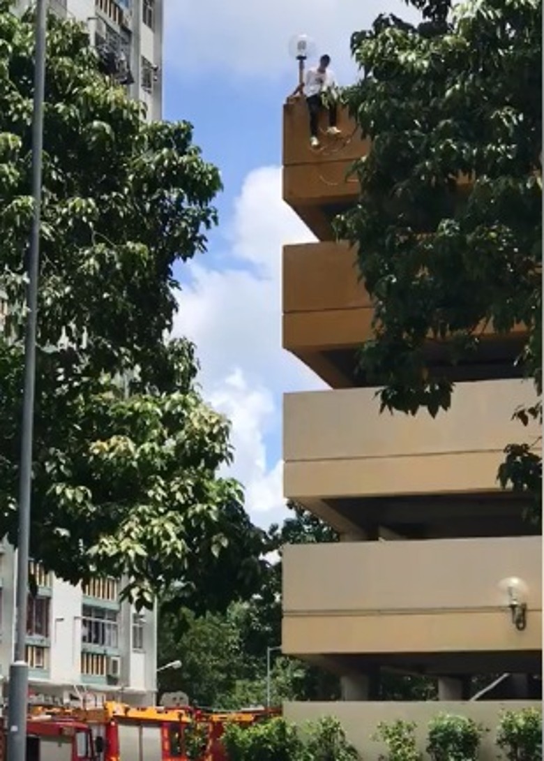 Middle aged man sits precariously on top of Wang Fuk Court Car Park in ...